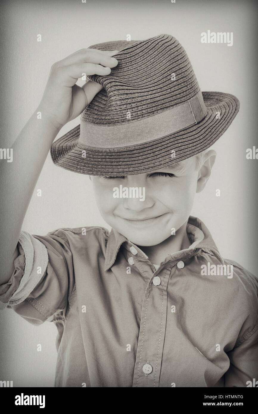 Closeup of a smiling little boy blinking holding a hat over white ...
