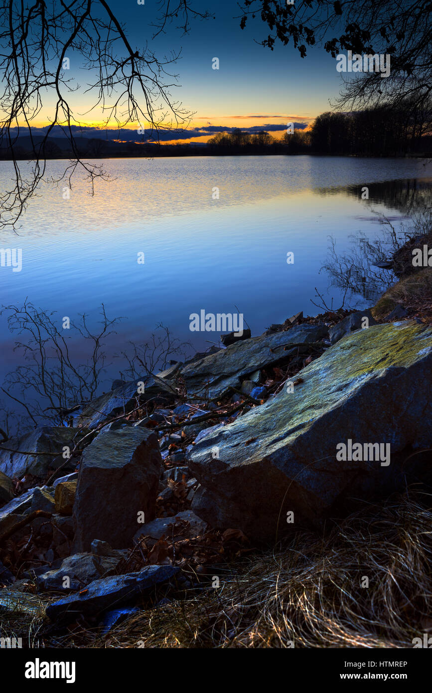 Lake with blue water and stone on the bank by sunset Stock Photo - Alamy