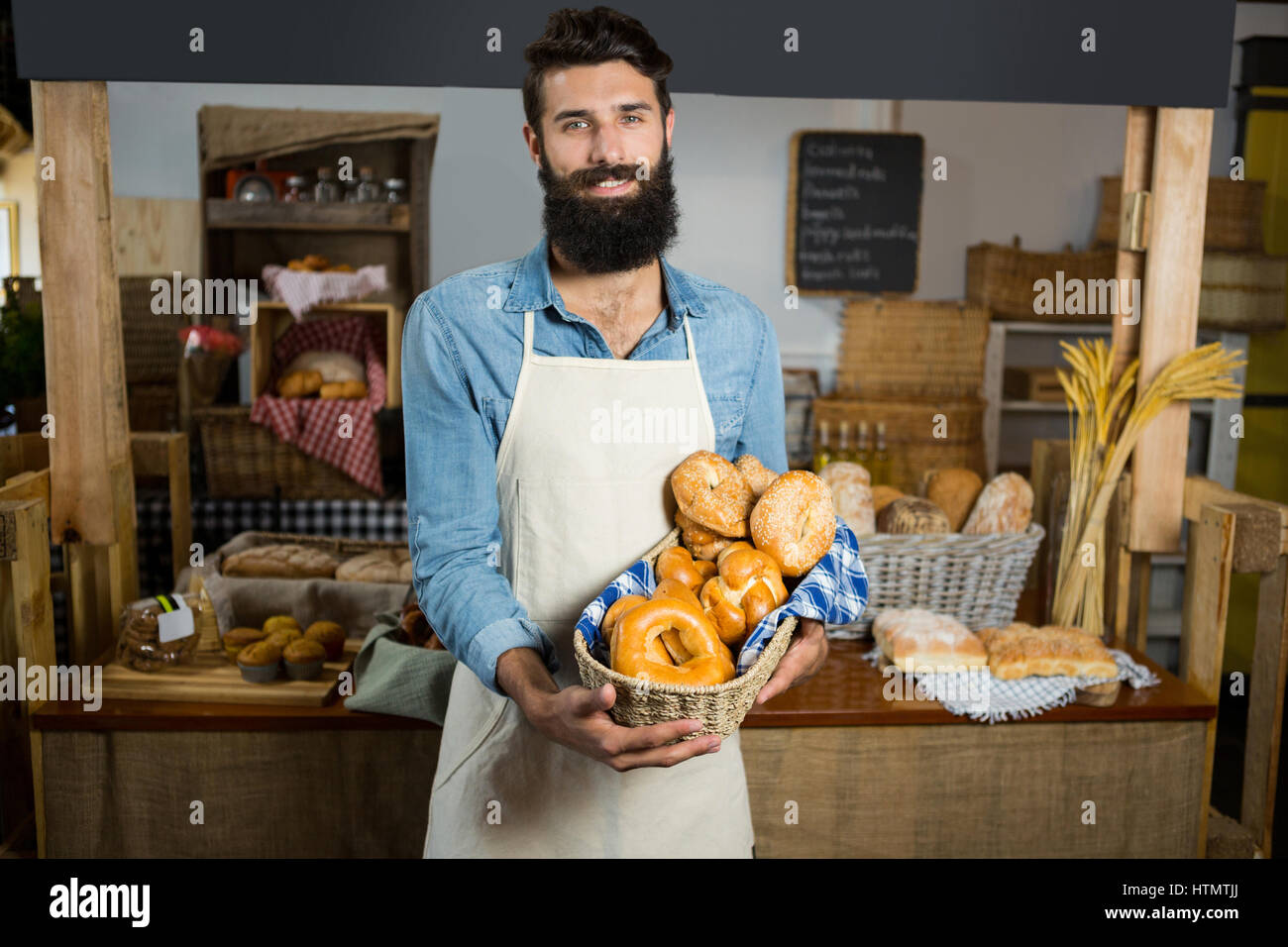 Portrait of smiling male staff holding a basket of bread at counter in ...