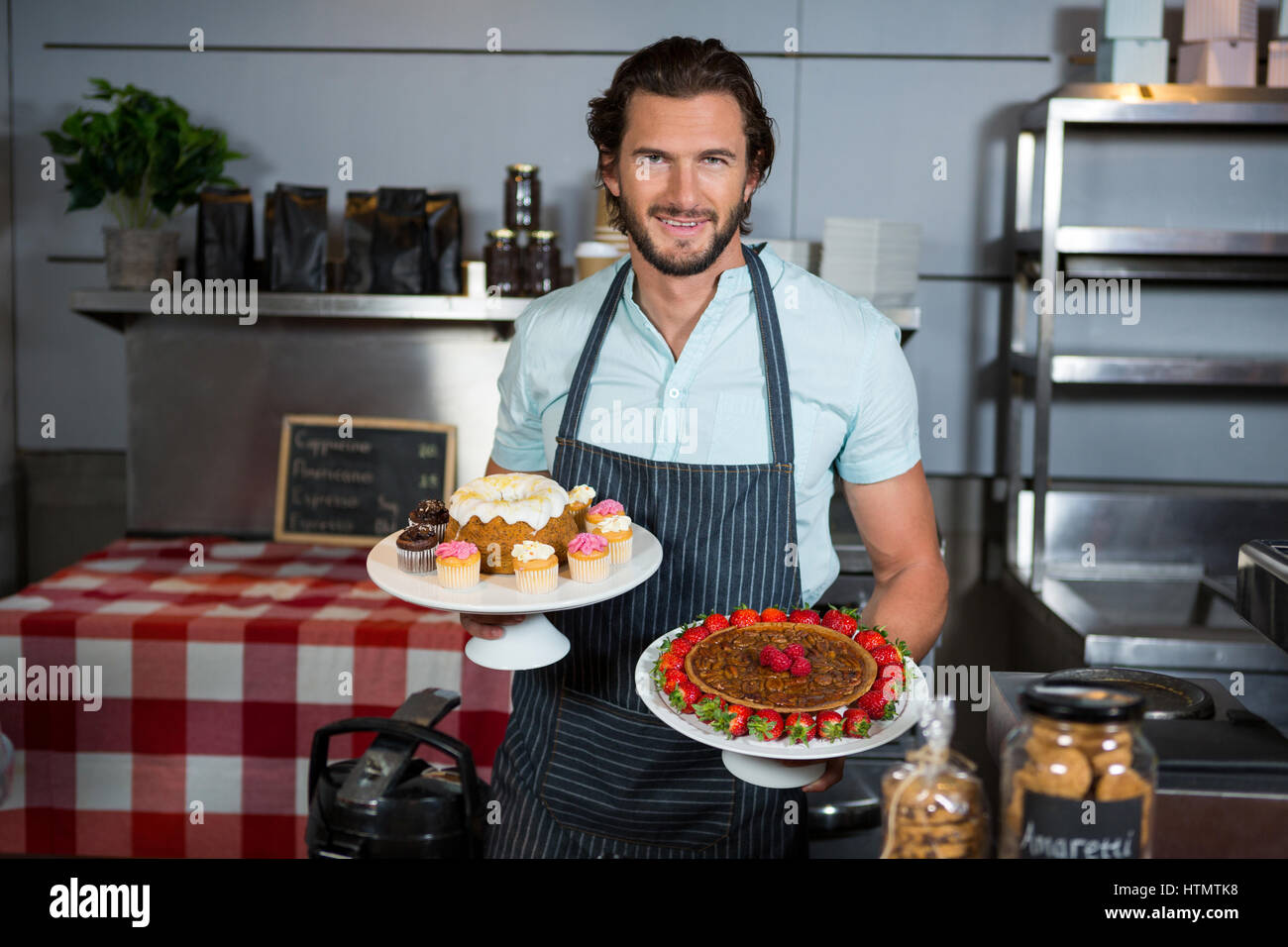 Portrait of male staff holding dessert on cake stand at counter in ...