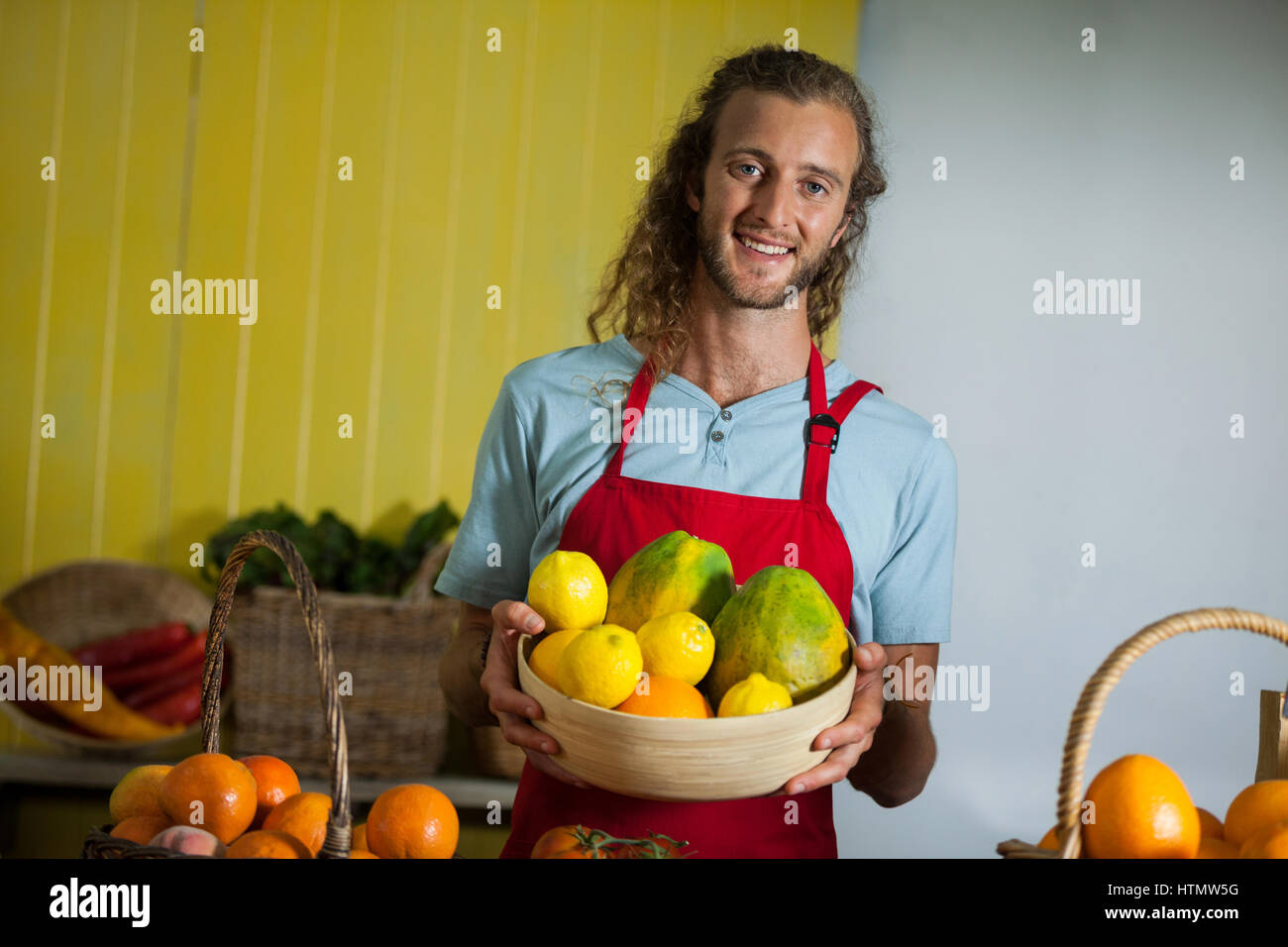 Smiling male staff holding fruits in basket at organic section of ...