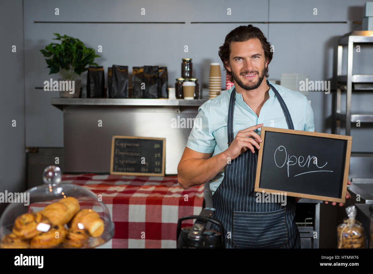Portrait of male staff holding a board with open sign in coffee shop ...