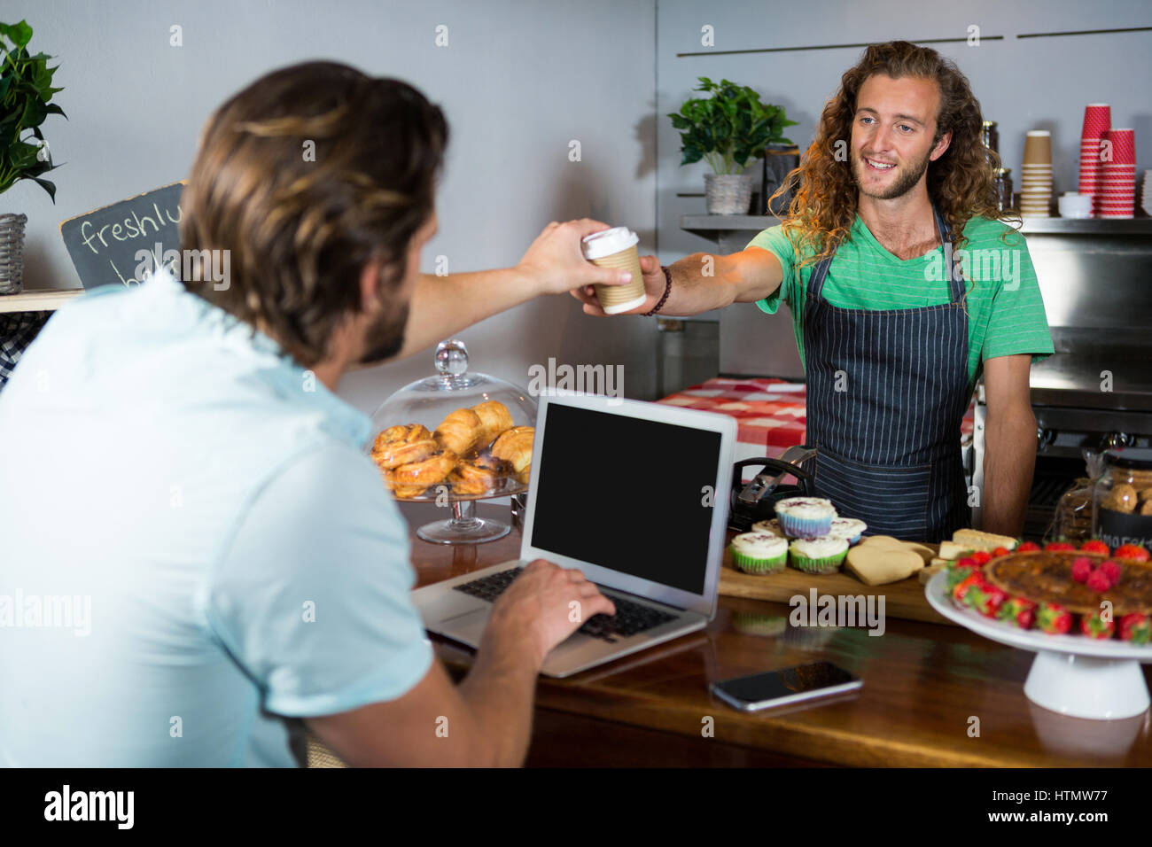 Customer receiving a coffee from staff at counter in coffee shop Stock ...