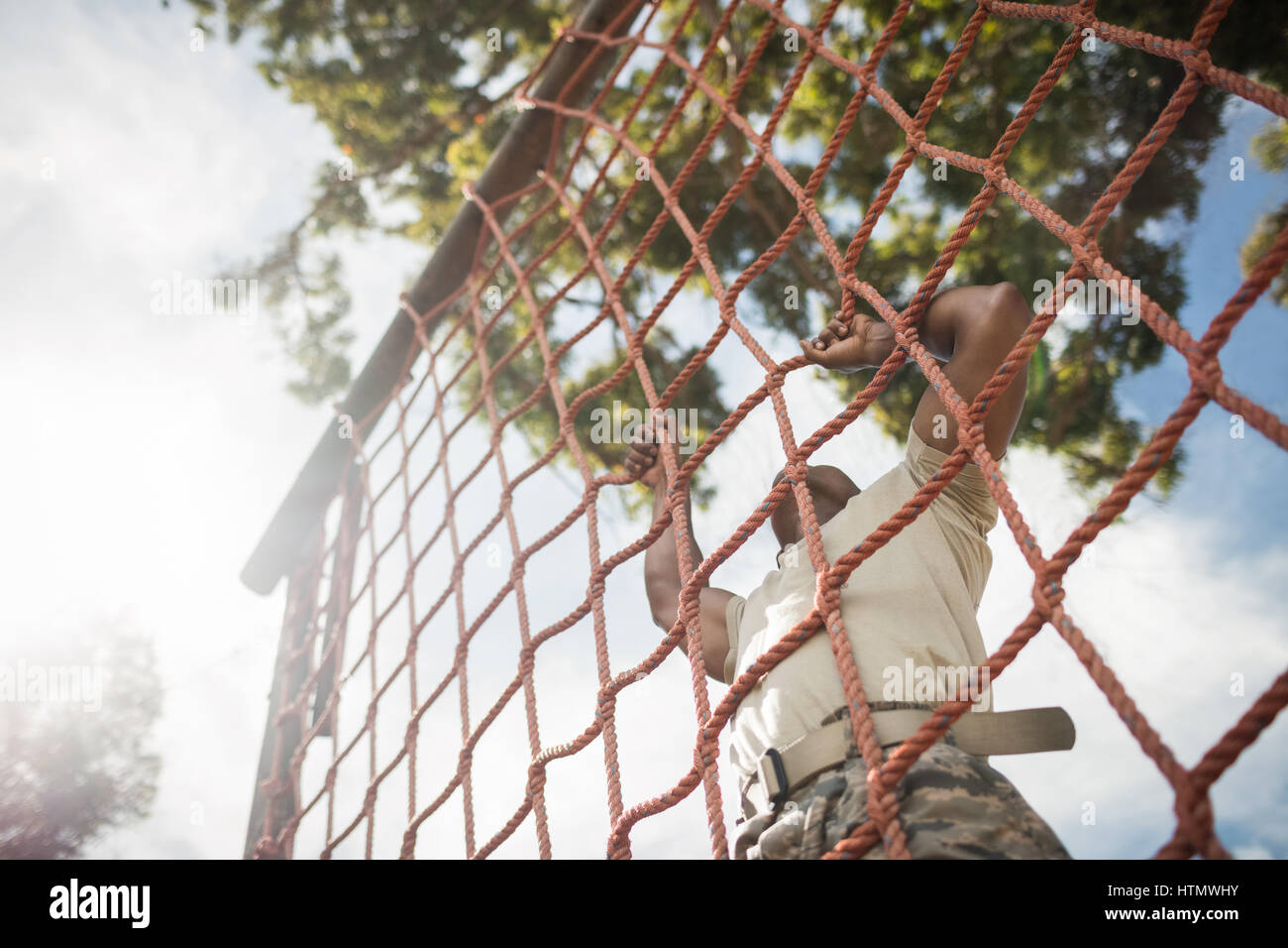 Military soldier climbing rope during obstacle course in boot camp ...