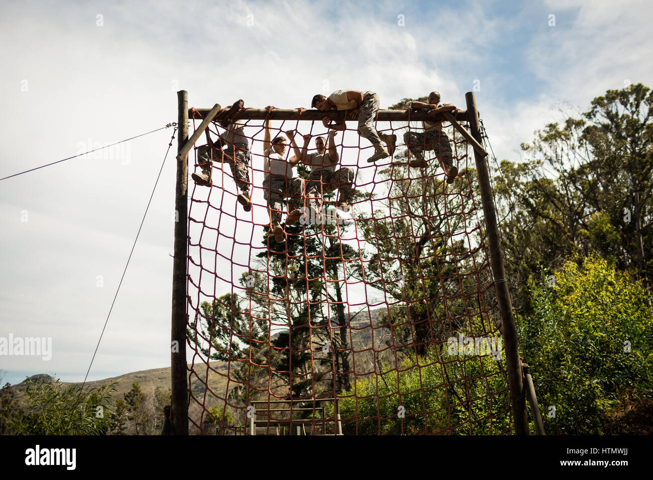 Military soldiers climbing rope during obstacle course in boot camp ...