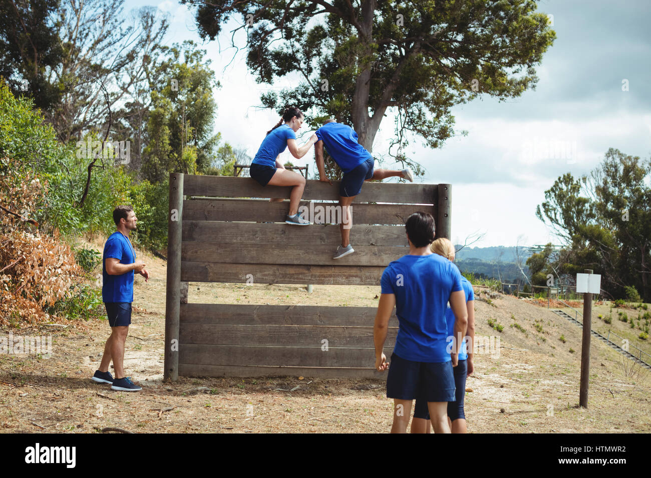 Female trainer assisting fit man to climb over wooden wall during ...
