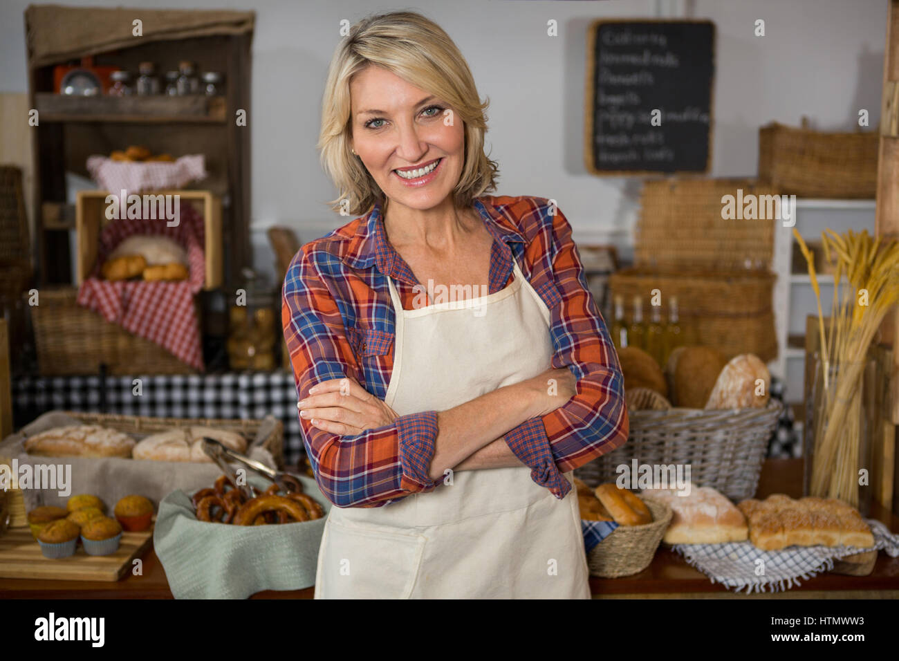Portrait of smiling female staff standing with arms crossed at counter ...