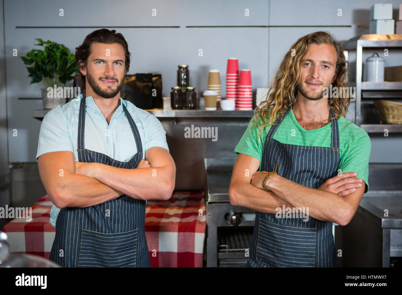 Portrait of smiling two male staff standing with arms crossed in coffee ...