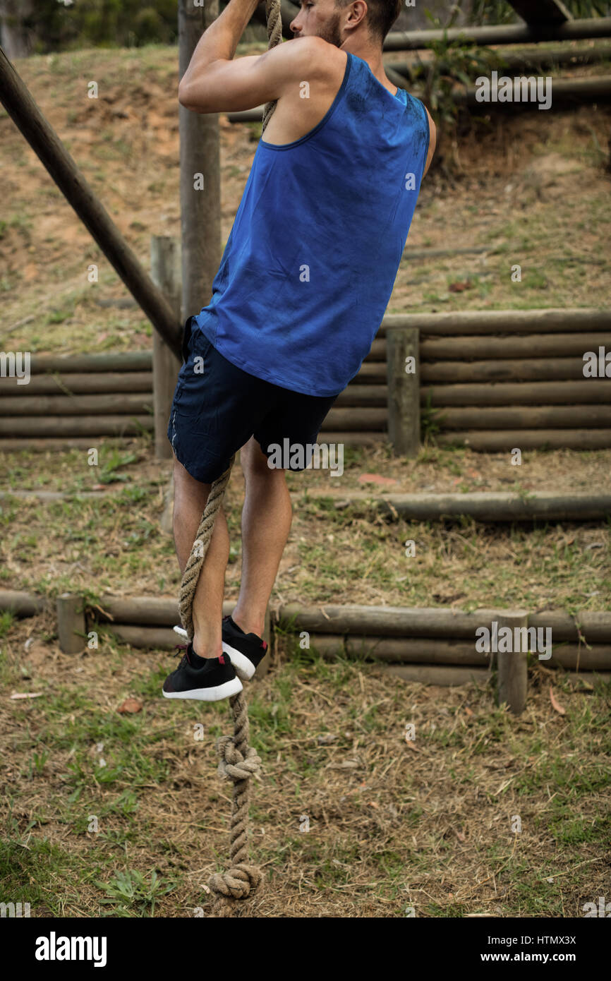 Fit man climbing a rope during obstacle course in boot camp Stock Photo ...