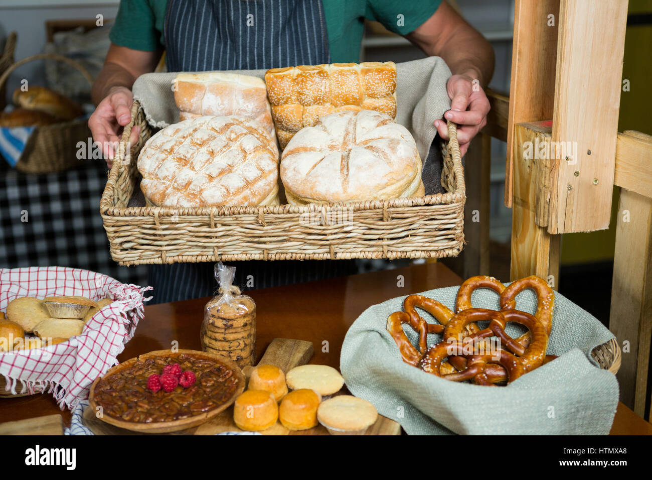 Mid section of male staff holding a basket of bread in bakery shop ...