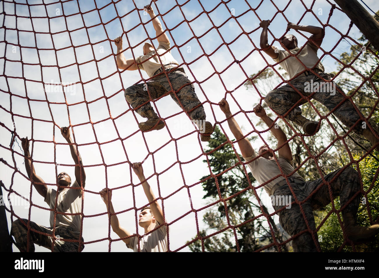 Military soldiers climbing rope during obstacle course in boot camp ...