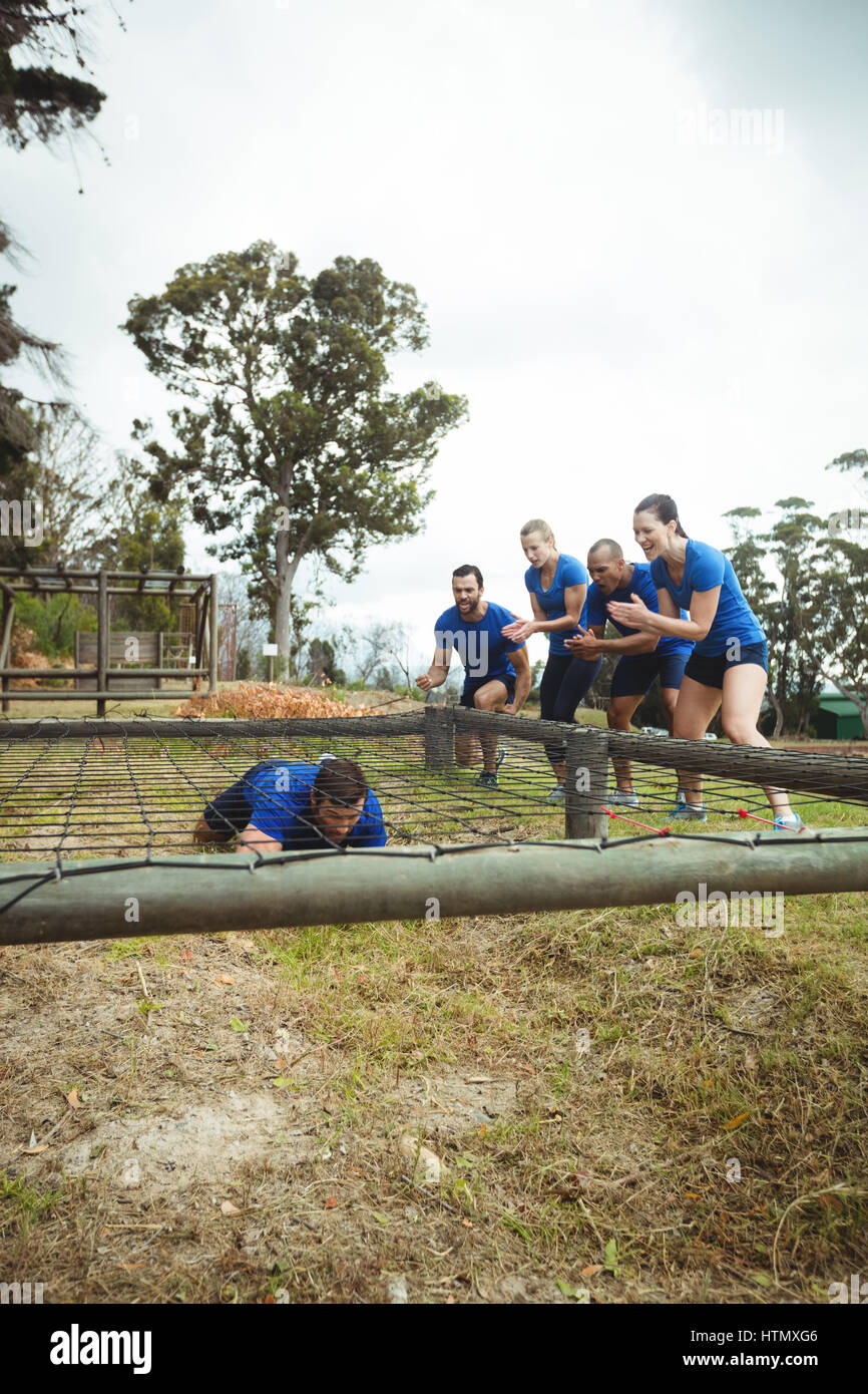 Fit man crawling under the net during obstacle course while fit people ...
