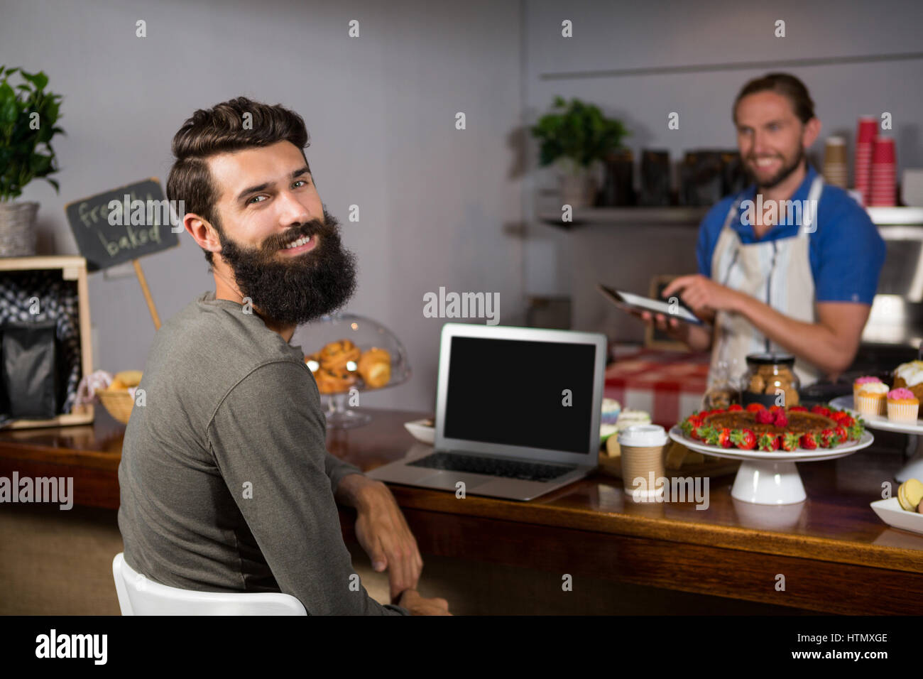 Smiling male customer using laptop while having coffee at counter in ...