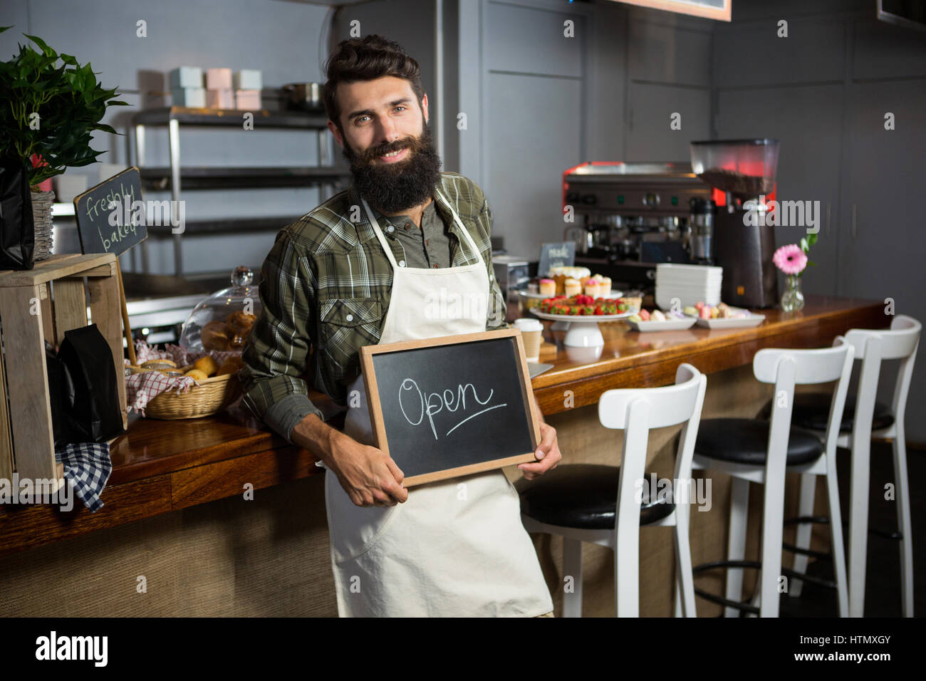 Portrait of smiling male staff holding chalkboard with open sign at ...
