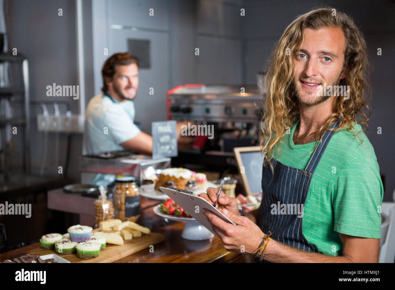Portrait of male staff writing on clipboard at counter in coffee shop ...