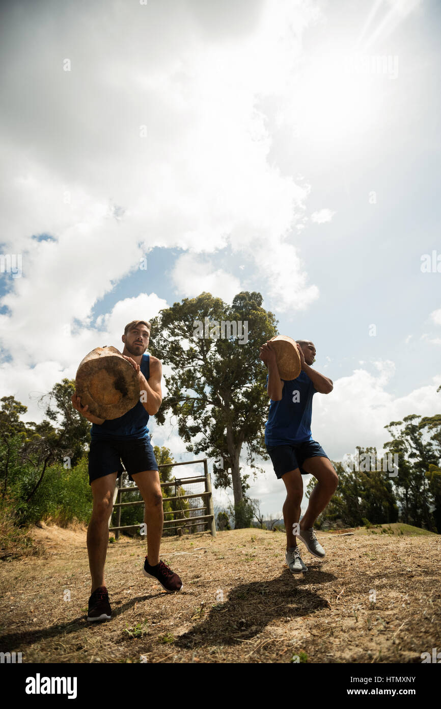 Fit men lifting heavy wooden logs during obstacle course in boot camp ...