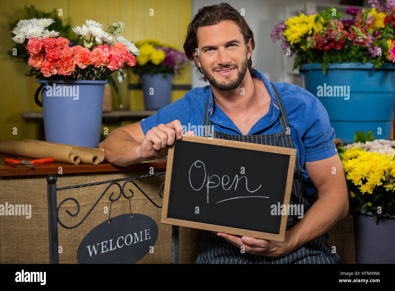 Portrait of male staff holding a board with open sign in flower shop ...