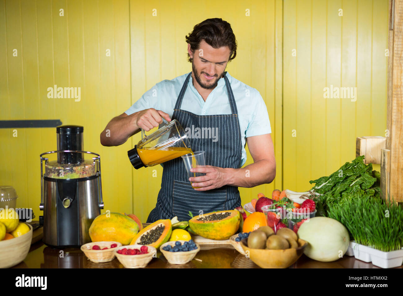 Male staff pouring juice into glass at counter in health grocery shop ...