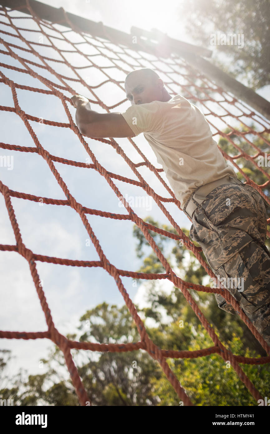 Military soldier climbing rope during obstacle course in boot camp ...