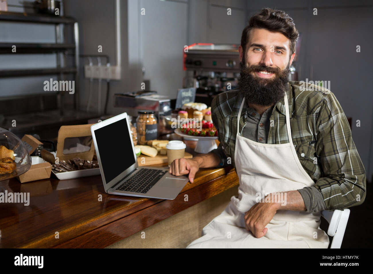 Portrait of smiling male staff using laptop at counter in in coffee ...