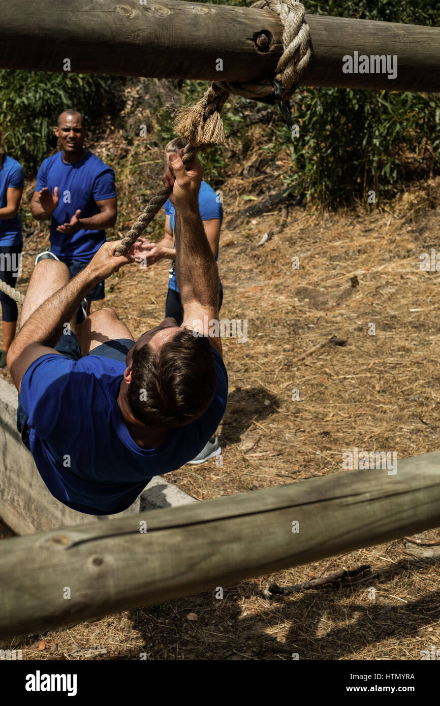 Fit man crossing the rope during obstacle course while people cheering ...