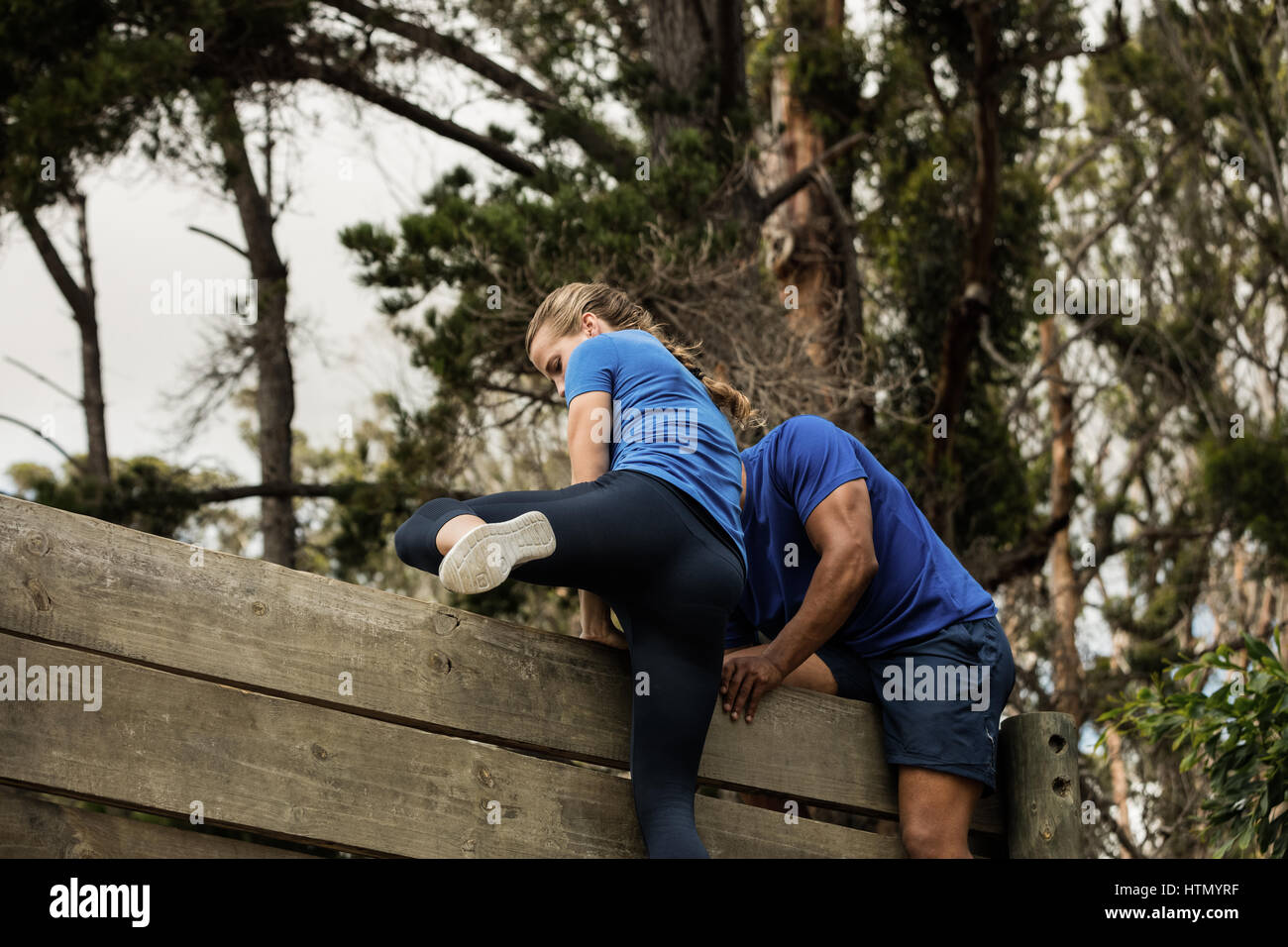 Male trainer assisting woman to climb a wooden wall during obstacle ...