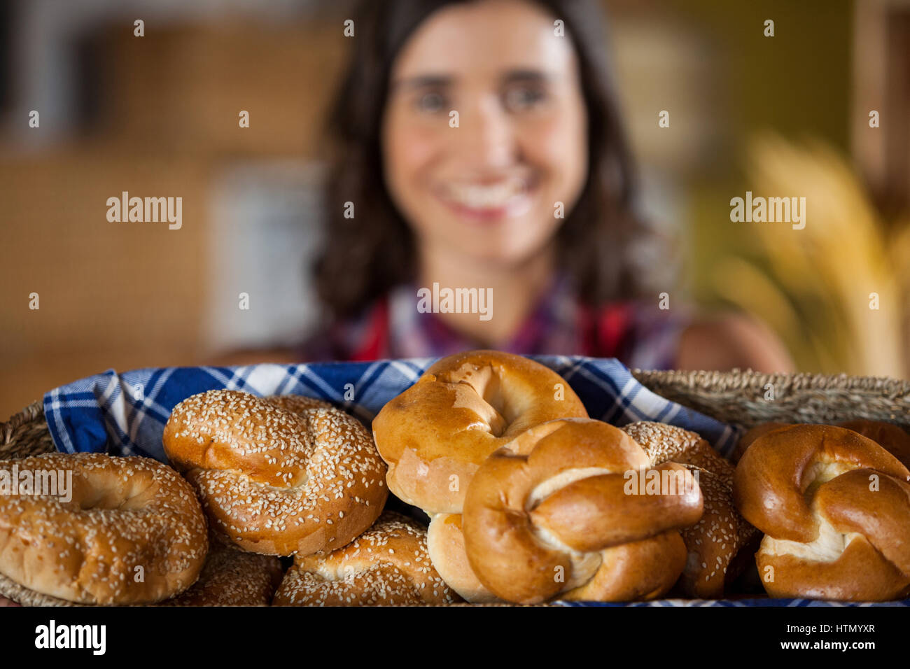 Smiling female staff holding wicker basket of various breads at counter ...