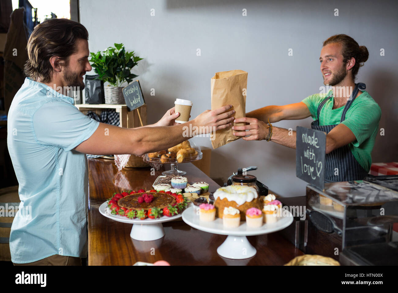 Smiling customer receiving a parcel from staff at counter in coffee ...