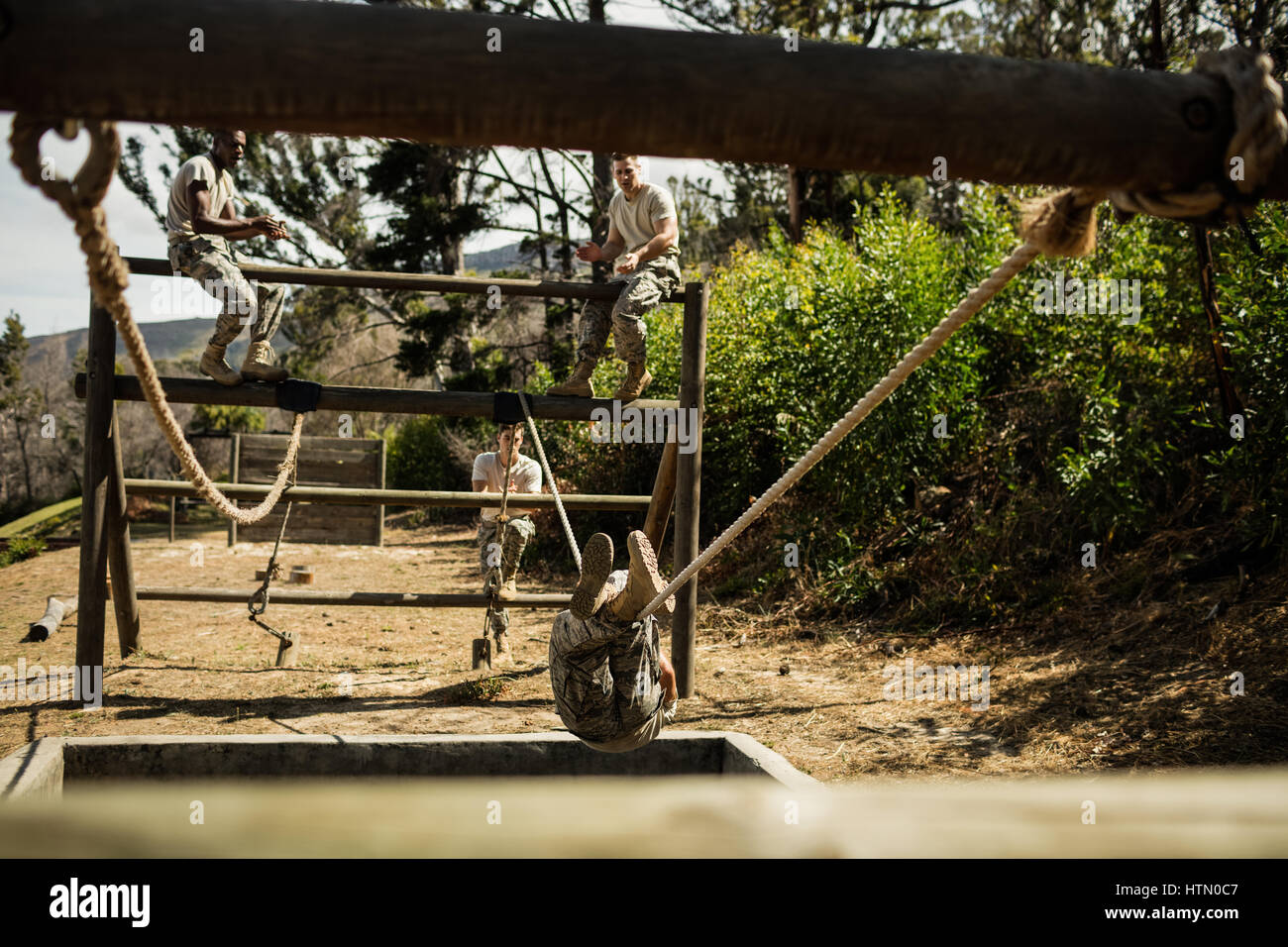 Young military soldiers practising rope climbing during obstacle course ...