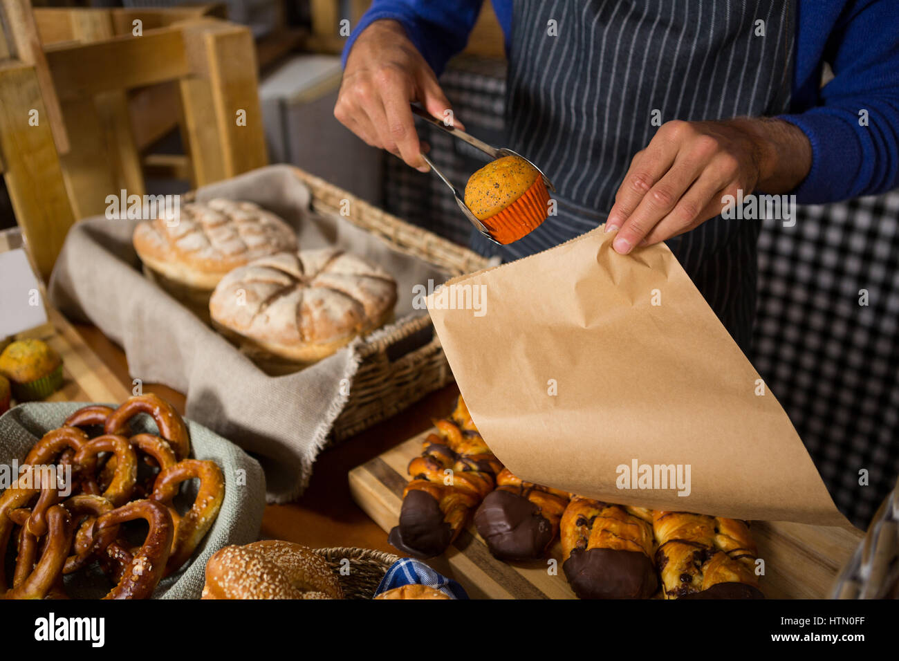 Mid section of staff packing cup cake in paper bag at counter in bakery ...