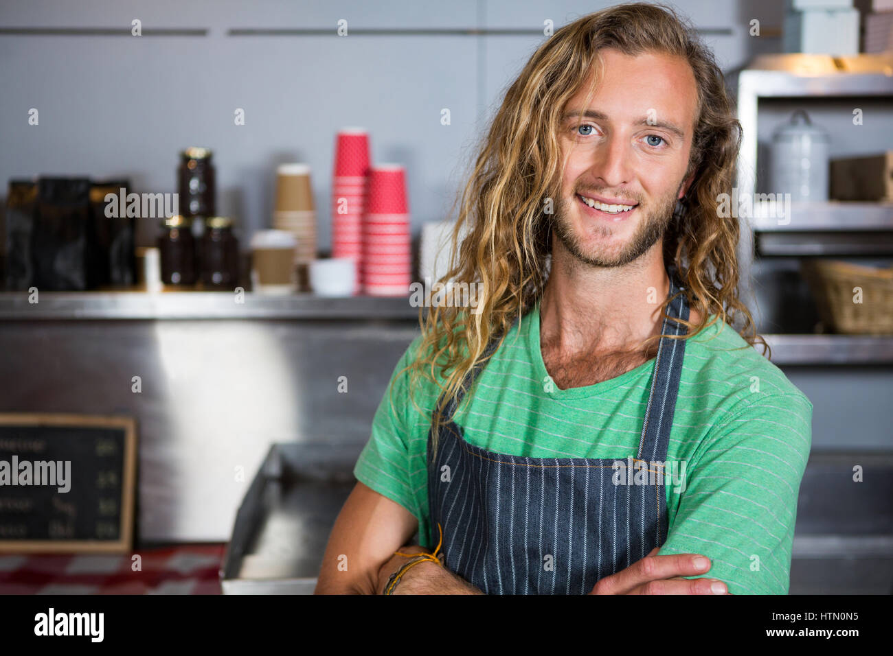 Portrait of smiling male staff standing with arms crossed in coffee ...