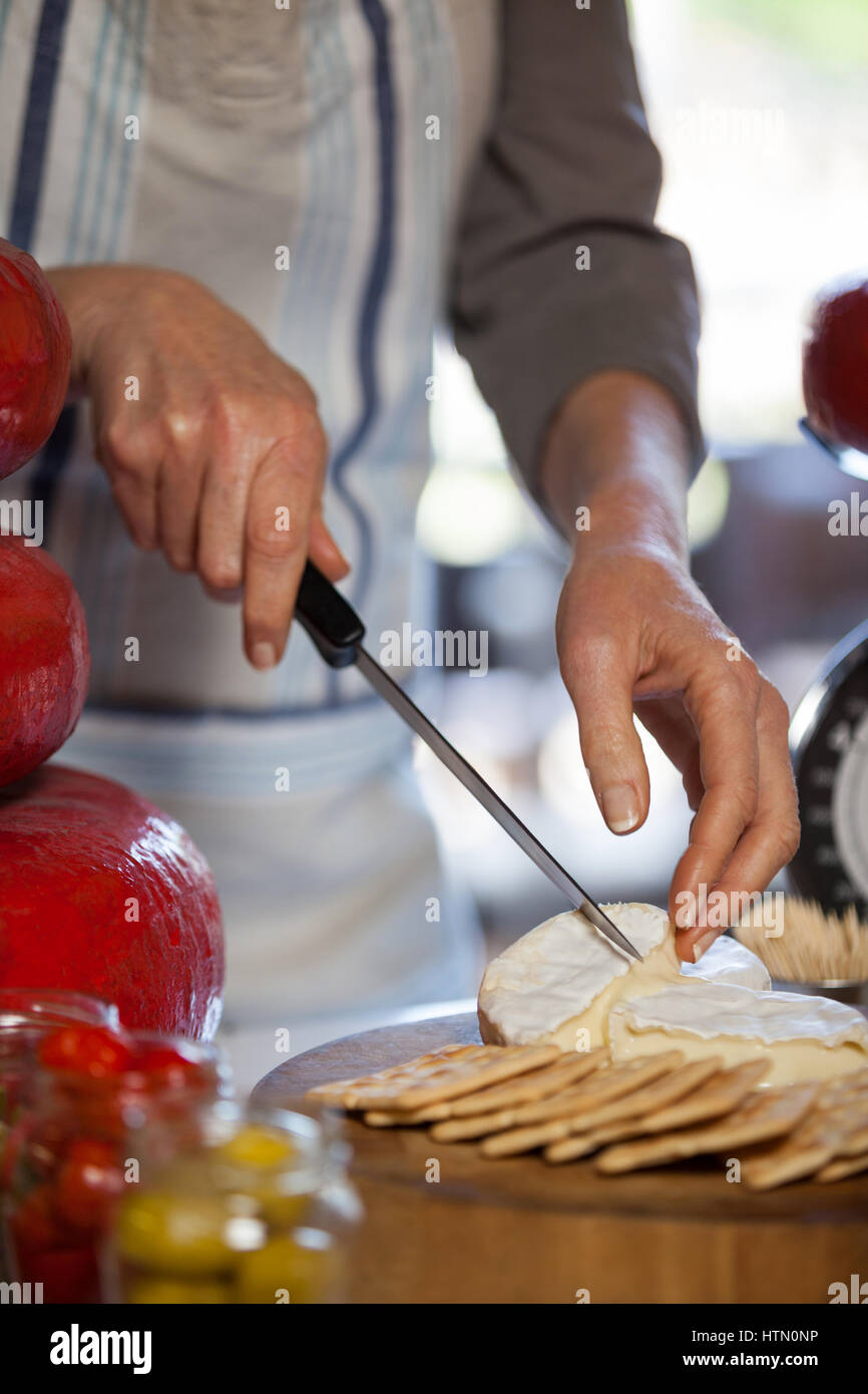 Mid section of female staff slicing cheese at counter of supermarket ...