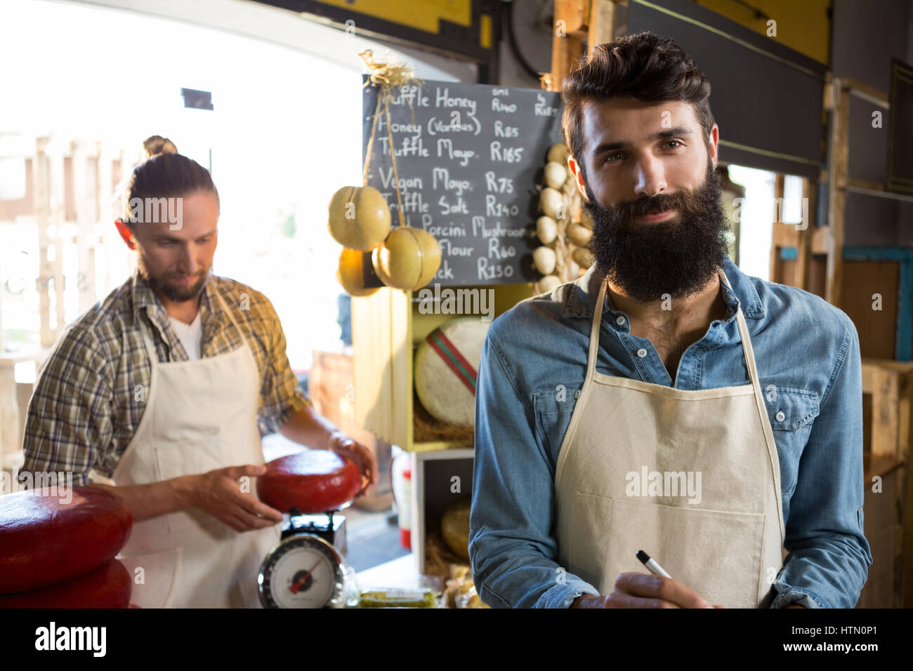 Portrait of salesman writing on clipboard at counter in grocery shop ...