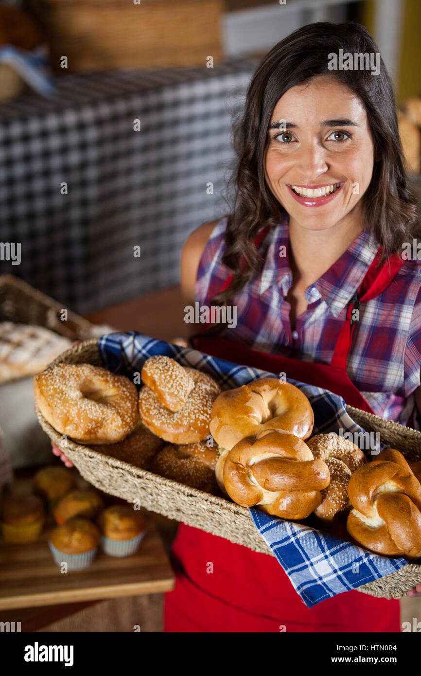 Smiling female staff holding wicker basket of various breads at counter ...