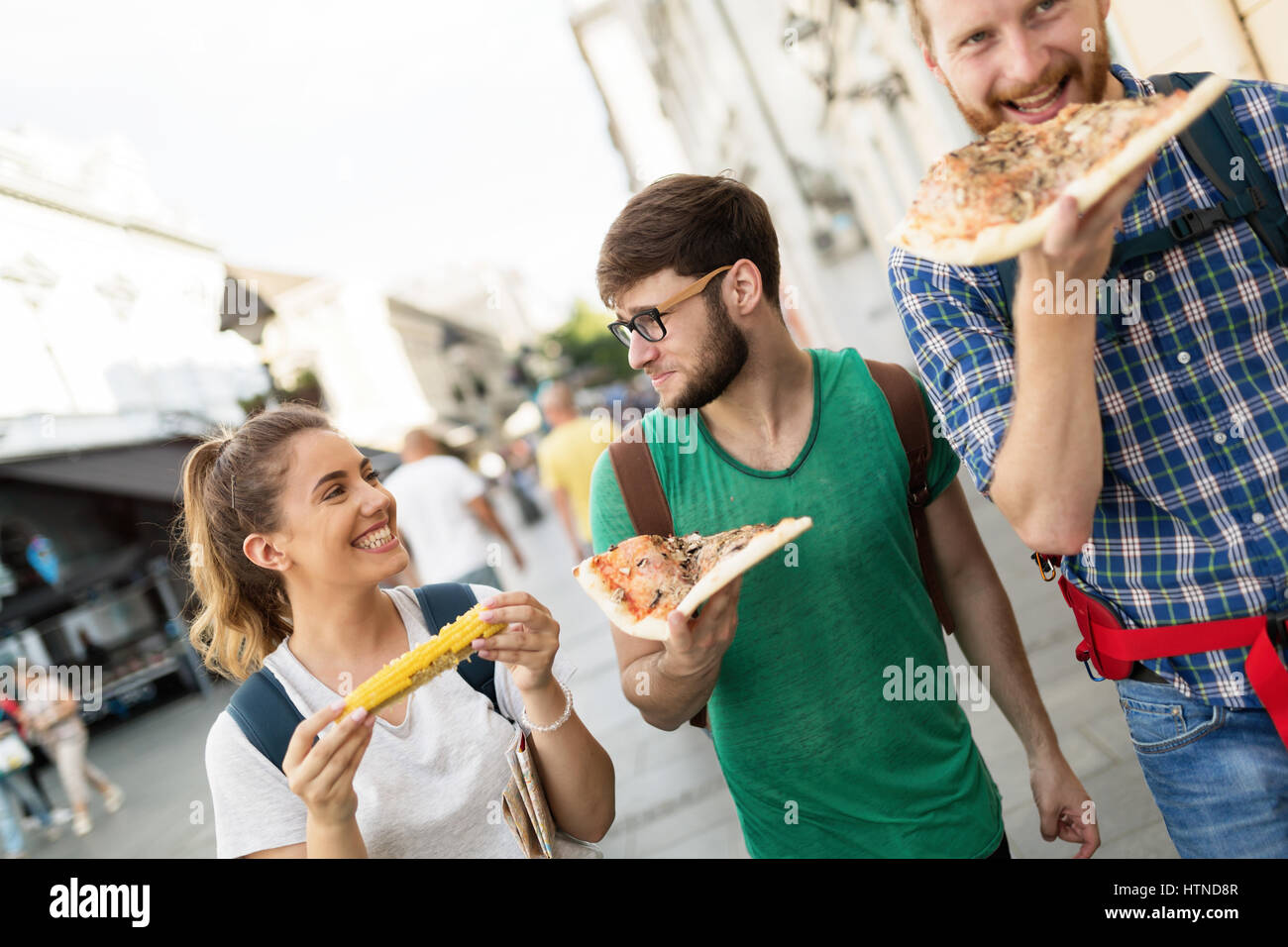 Happy people eating fast food in city while travelling with backpacks ...