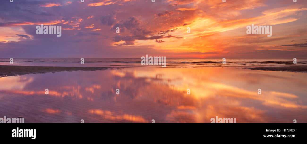 Spectacular sunset colours over sea reflected in the water at low tide ...