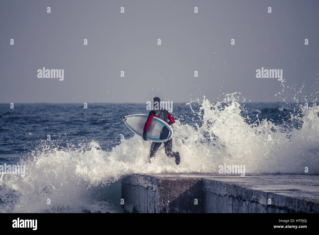 Surfer runs into water wearing a wetsuit in winter. Cold surfing. Wave ...