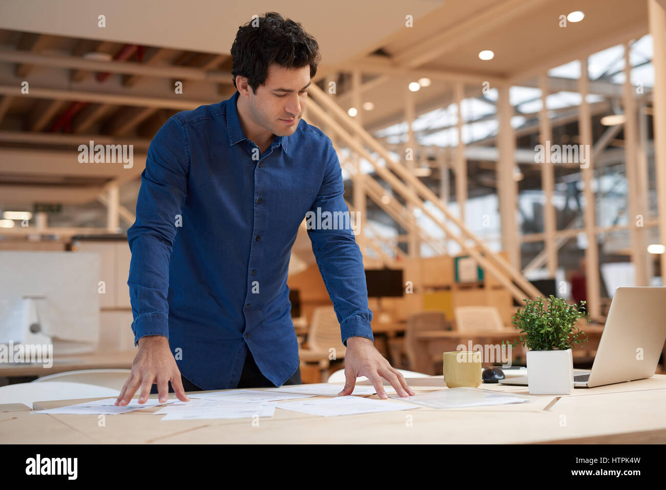 Casually dressed focused young businessman leaning over a desk in a ...