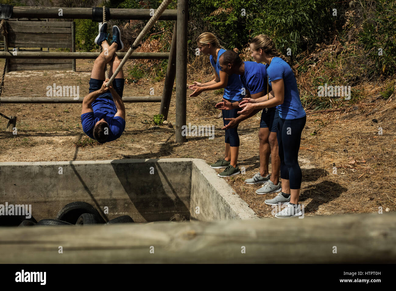 Fit man crossing the rope during obstacle course while people cheering ...