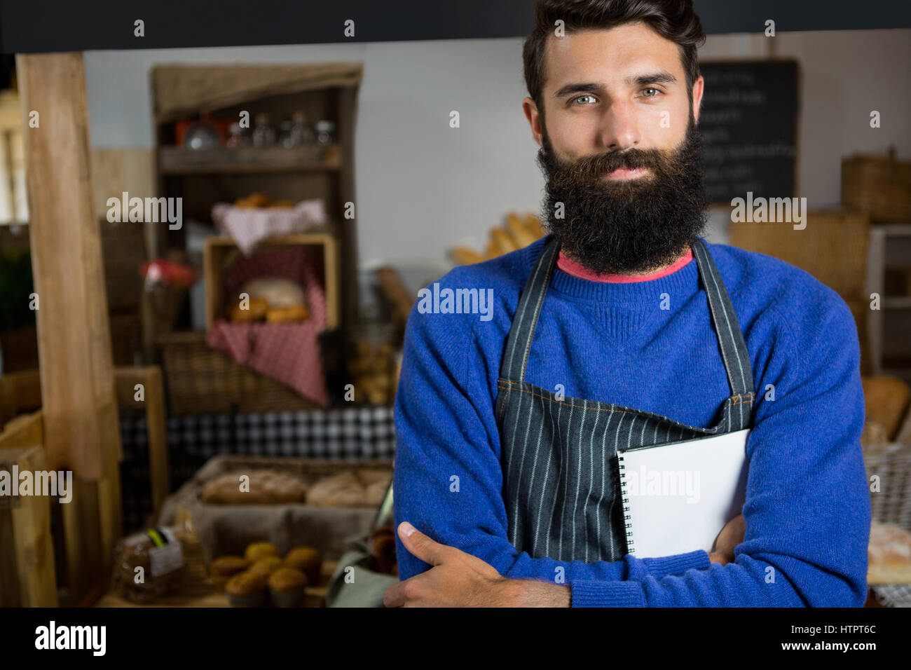 Portrait of male staff standing with arms crossed at counter in bakery ...