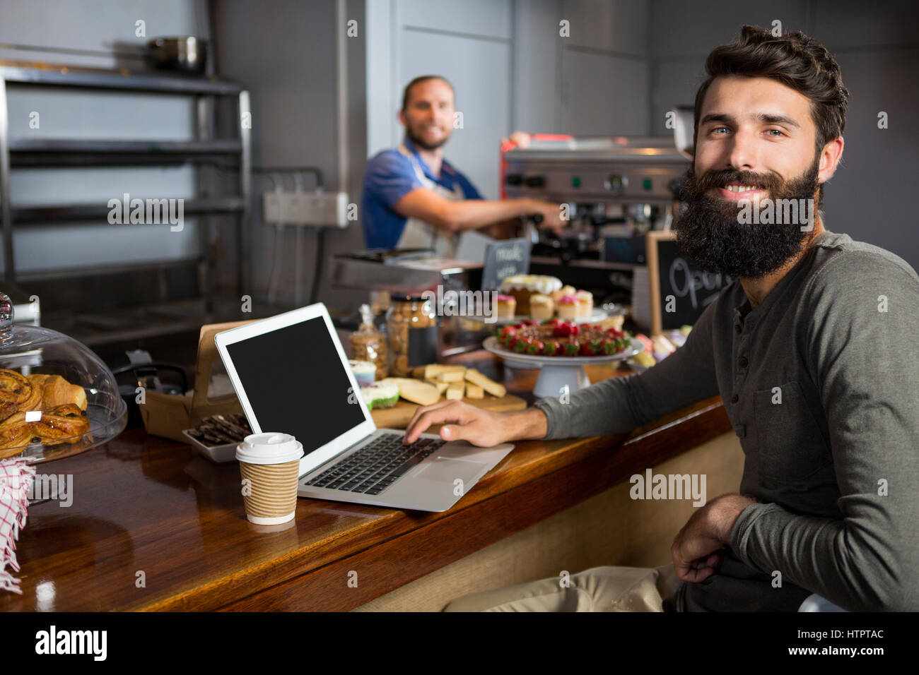 Smiling male customer using laptop while having coffee at counter in ...