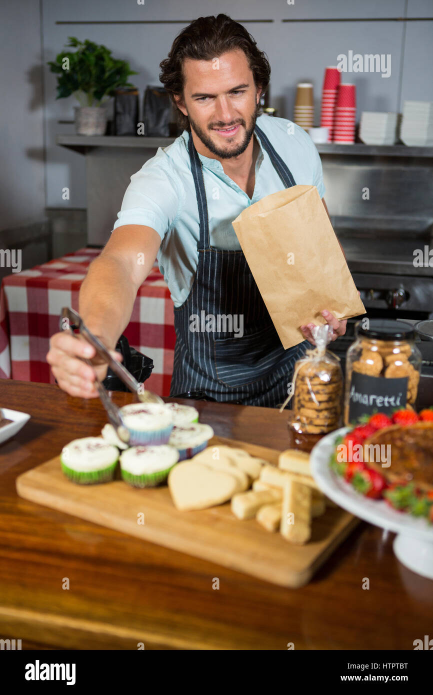 Staff packing a cup cake in paper bag at counter in coffee shop Stock ...
