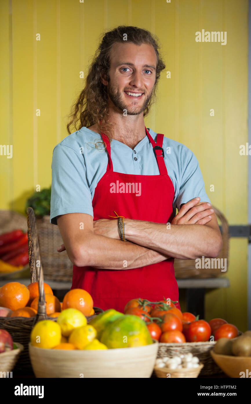 Smiling male staff standing with arms crossed in organic section of ...