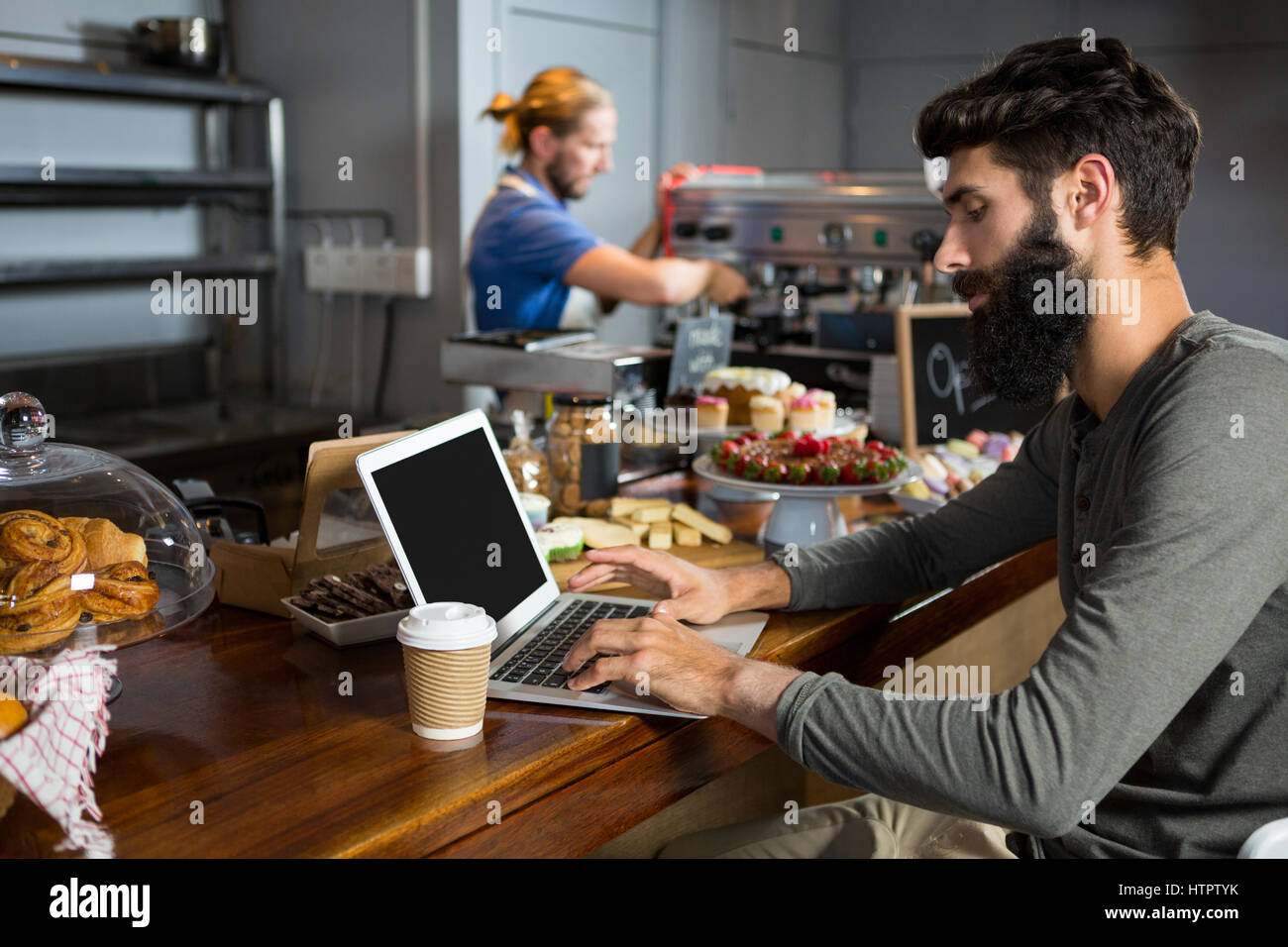 Male customer using laptop while having coffee at counter in coffee ...
