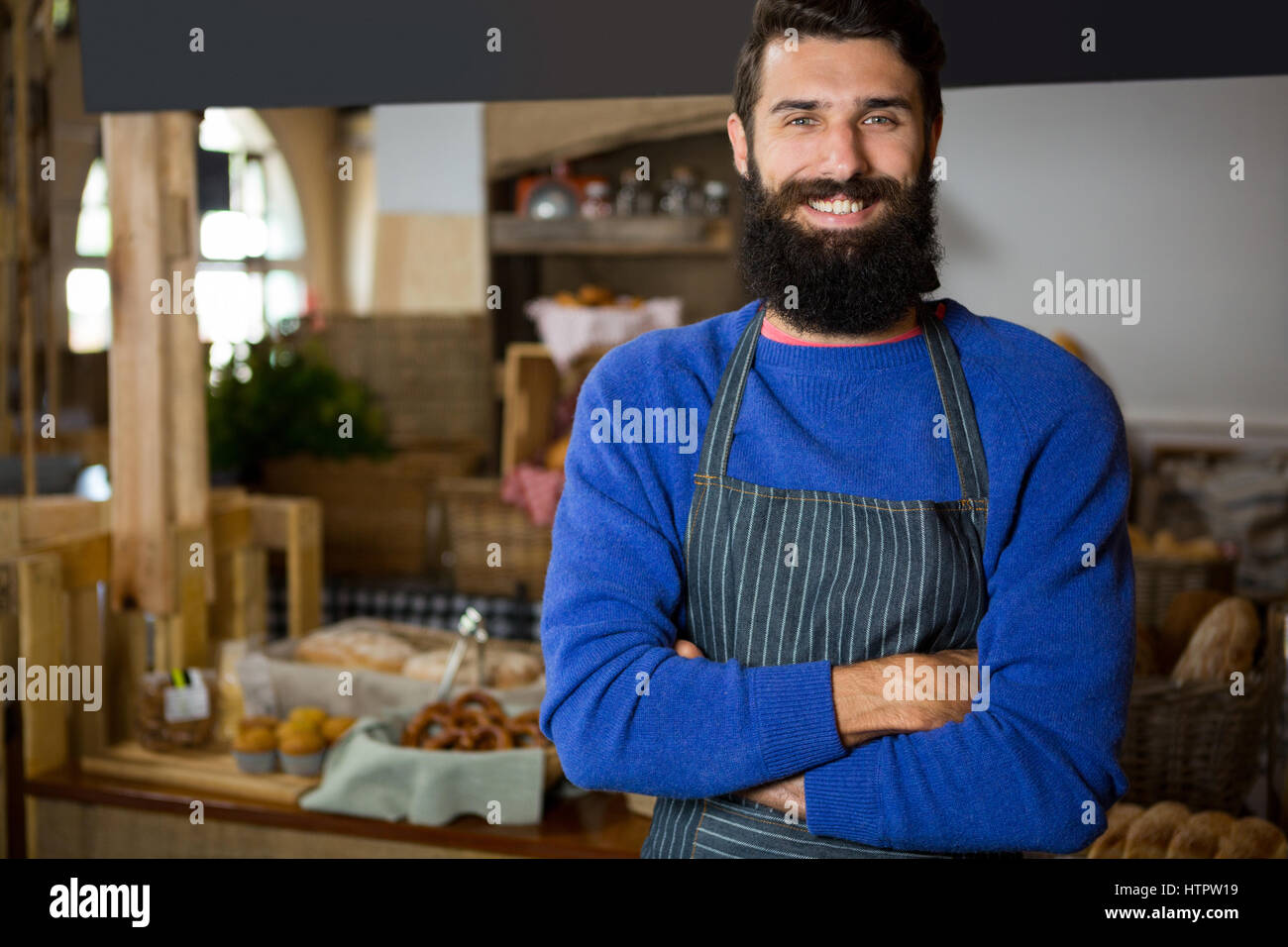 Portrait of smiling male staff standing with arms crossed at counter in ...
