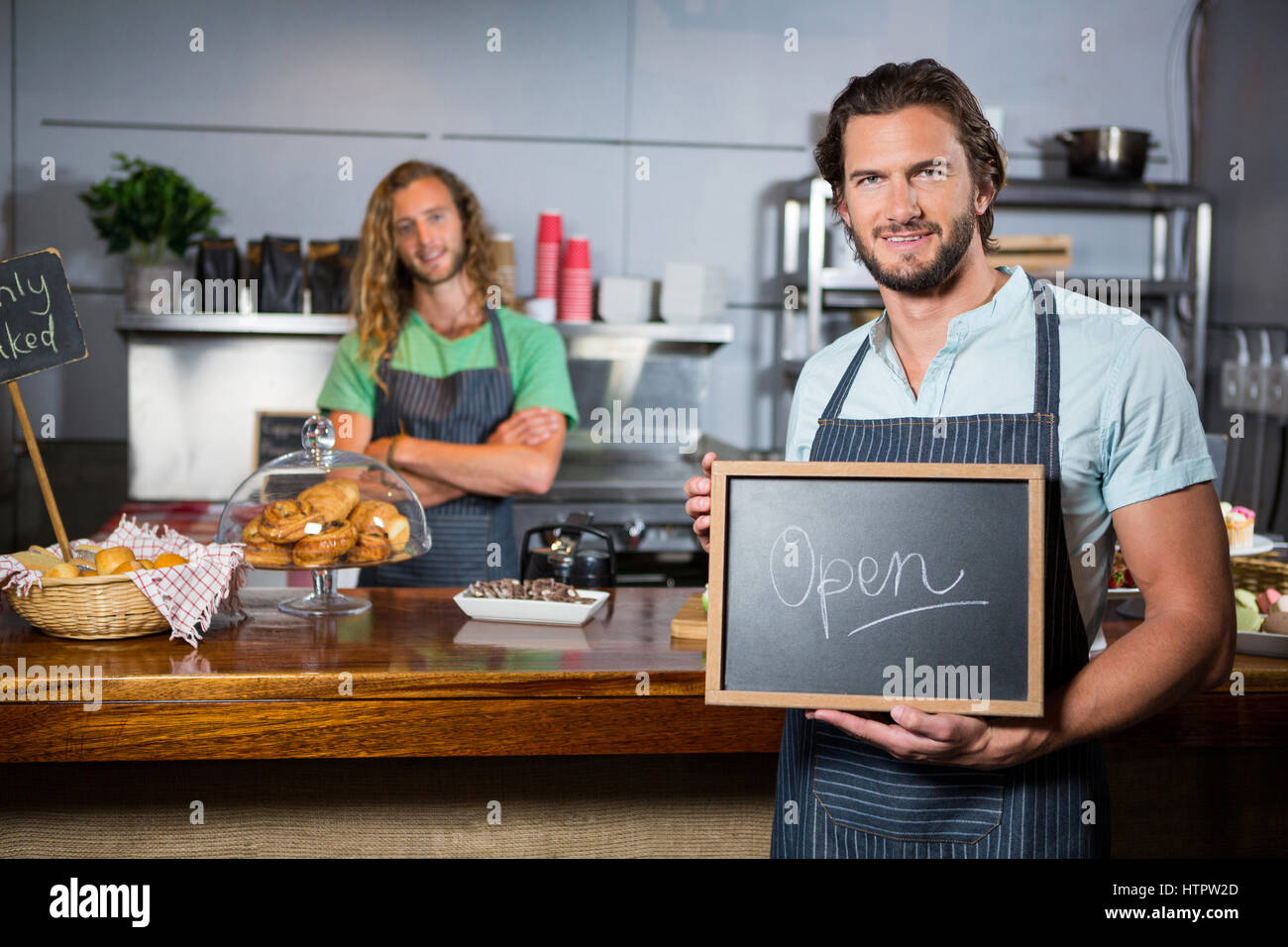 Portrait of Male staff holding a board with open sign and colleague ...