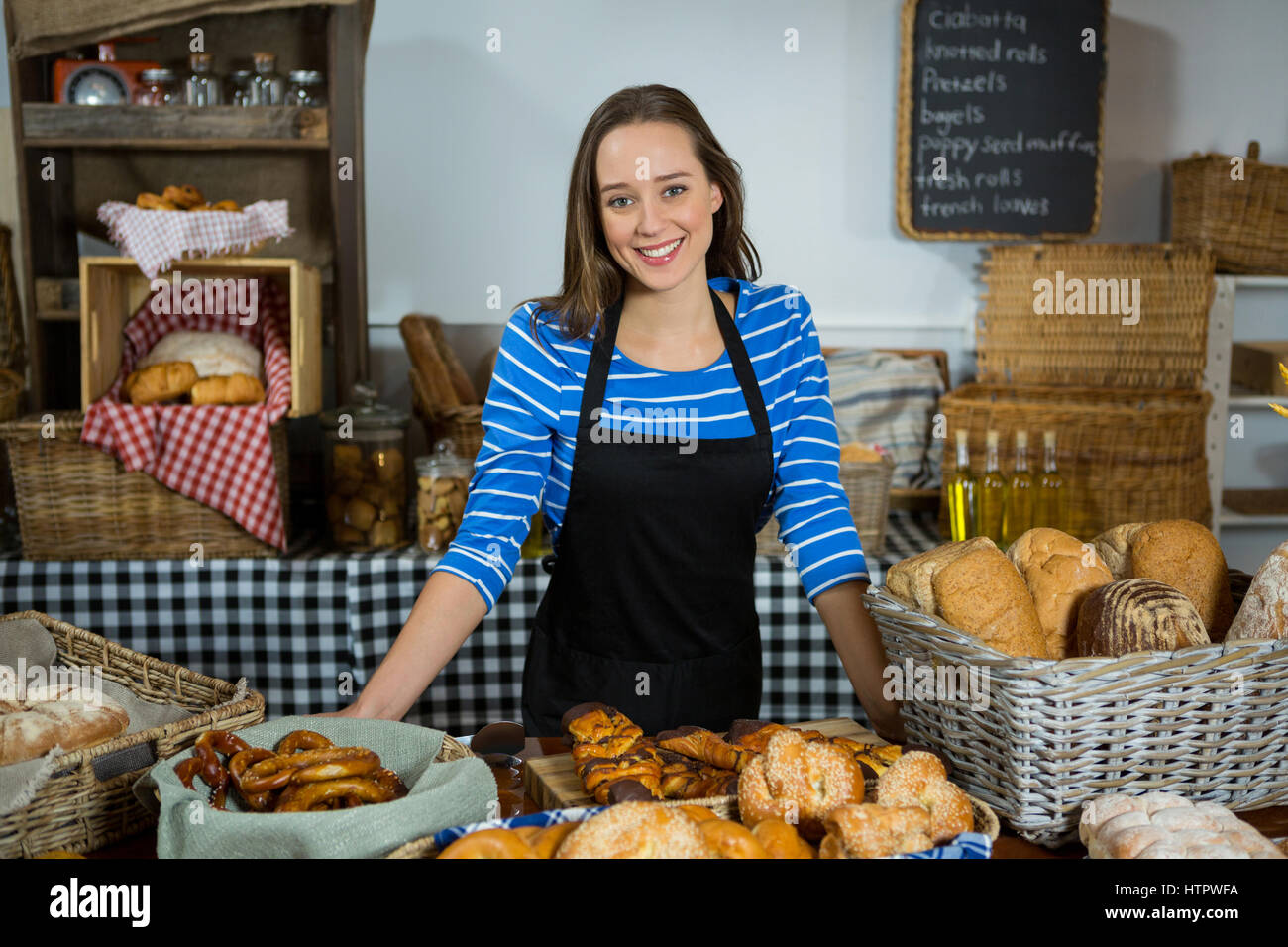 Portrait of smiling female staff standing at bread counter in bakery ...