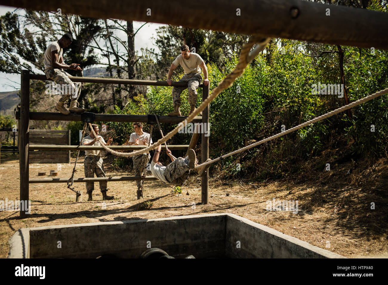 Young military soldiers practising rope climbing during obstacle course ...
