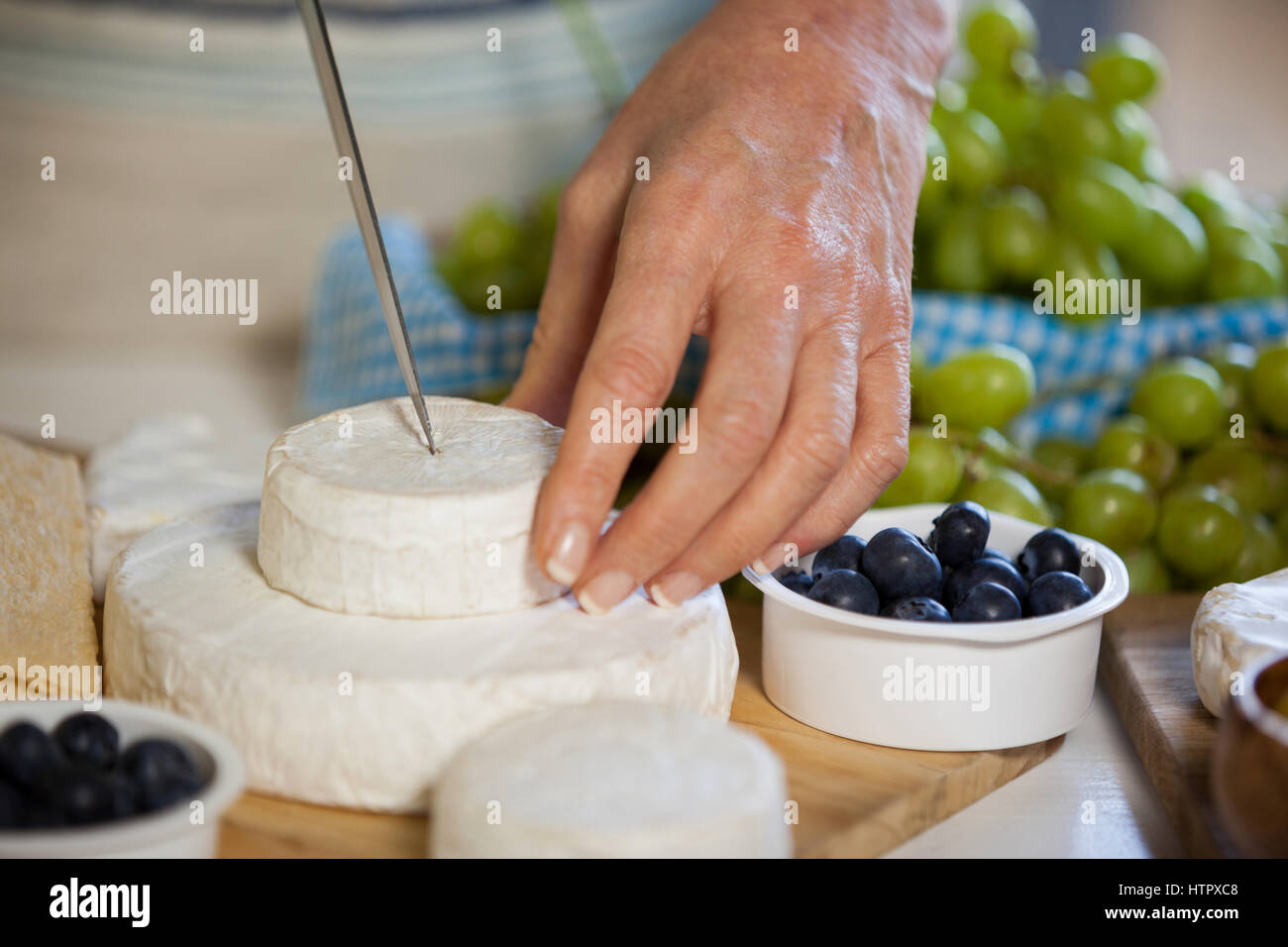 Mid section of female staff slicing cheese at counter of supermarket ...