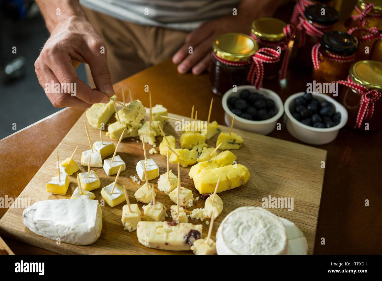 Close-up of staff arranging piece of cheese on wooden board in grocery ...
